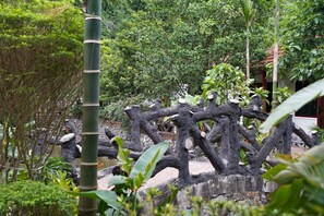 Um jardim naturalístico com uma escultura de tronco de árvore, vegetação exuberante e um caminho de pedra.