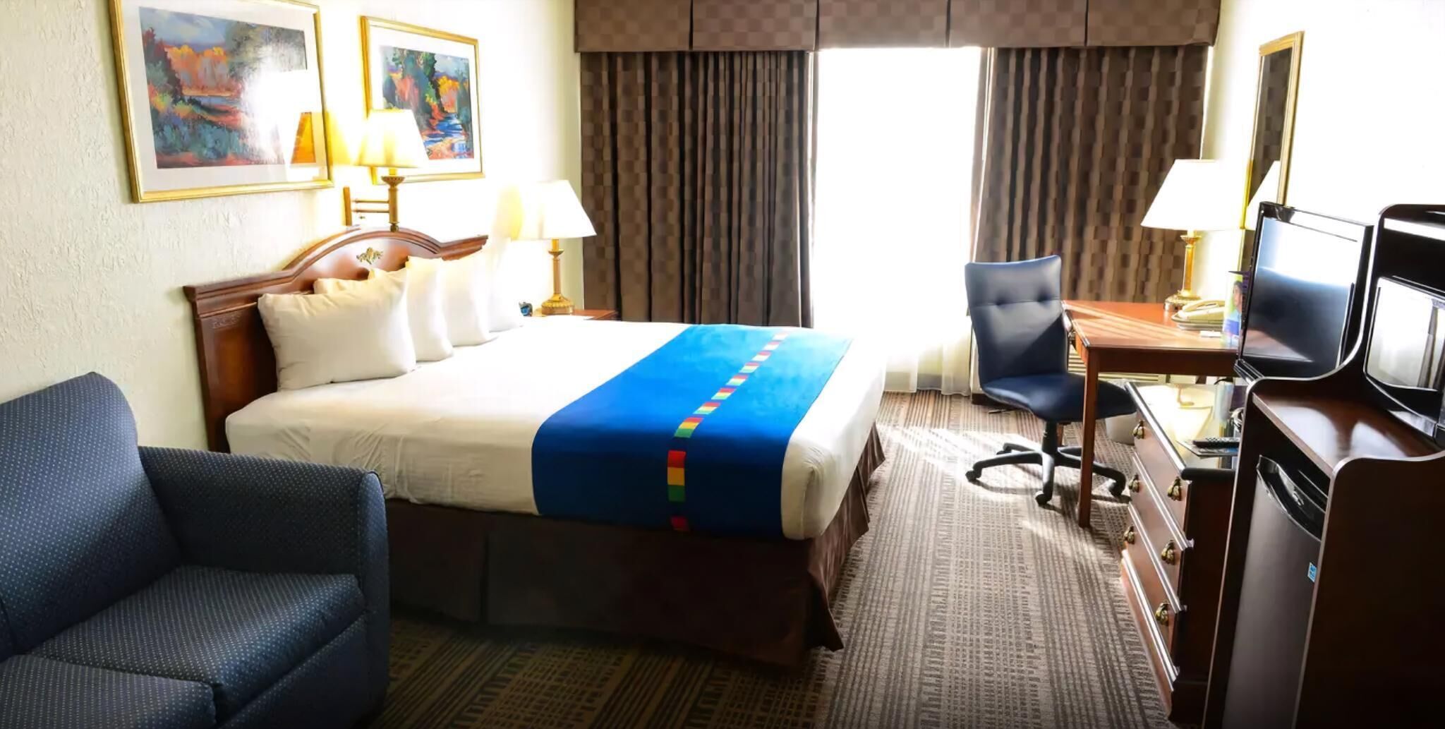 Quarto de hotel com cama, escrivaninha, cadeira, televisão e obras de arte nas paredes.