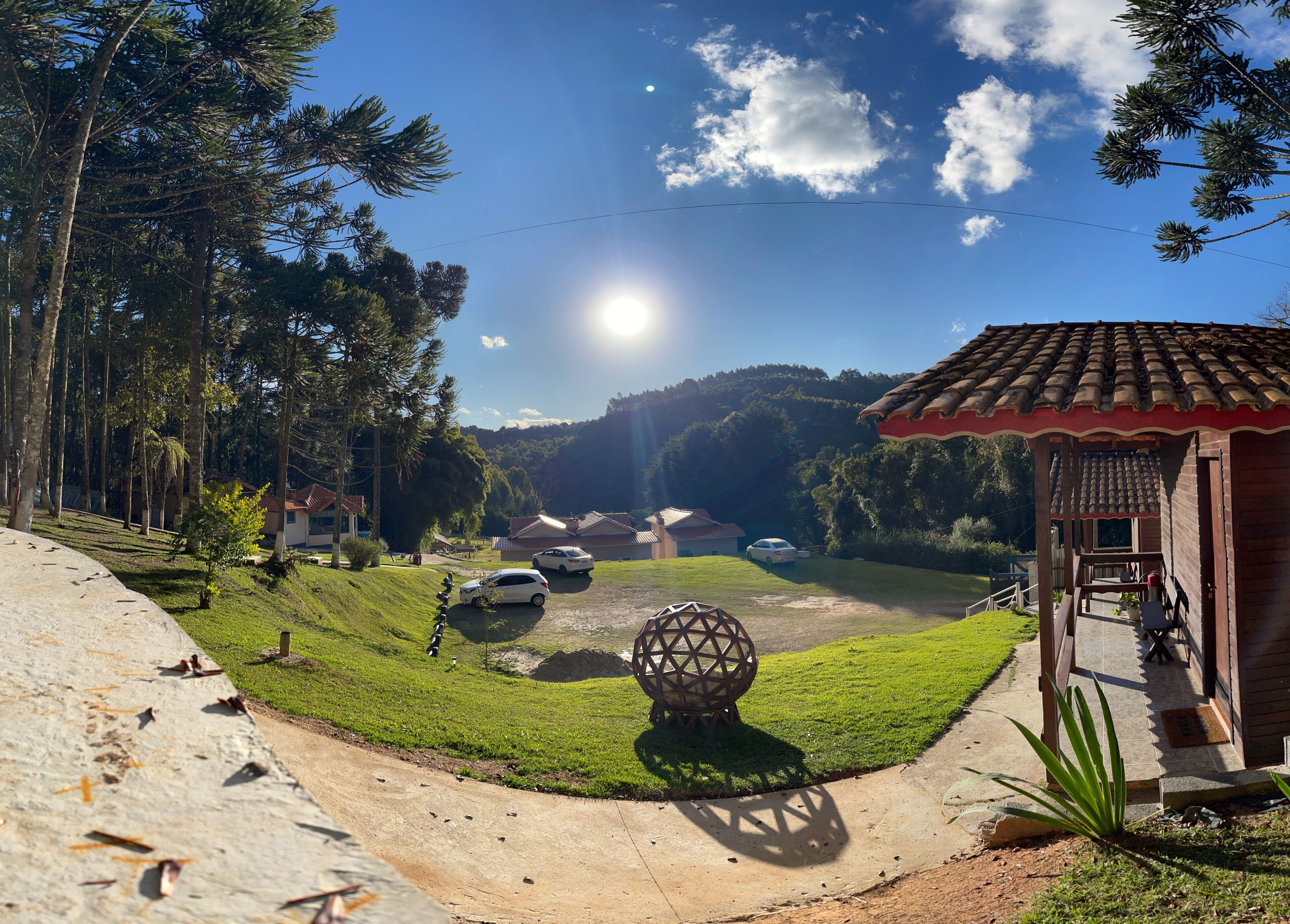 Paisagem rural sob um céu claro, com uma escultura esférica e um edifício tradicional com telhado de azulejos.