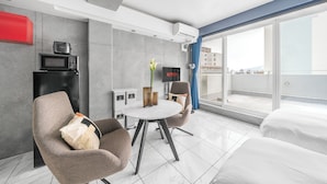 Quarto de hotel moderno com uma cama, dois poltronas, uma mesa pequena, micro-ondas, televisão e vista para a cidade.