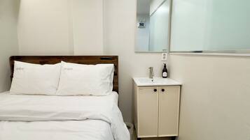 Quarto de hotel com uma cama, mesa de cabeceira com espelho e um pequeno armário.
