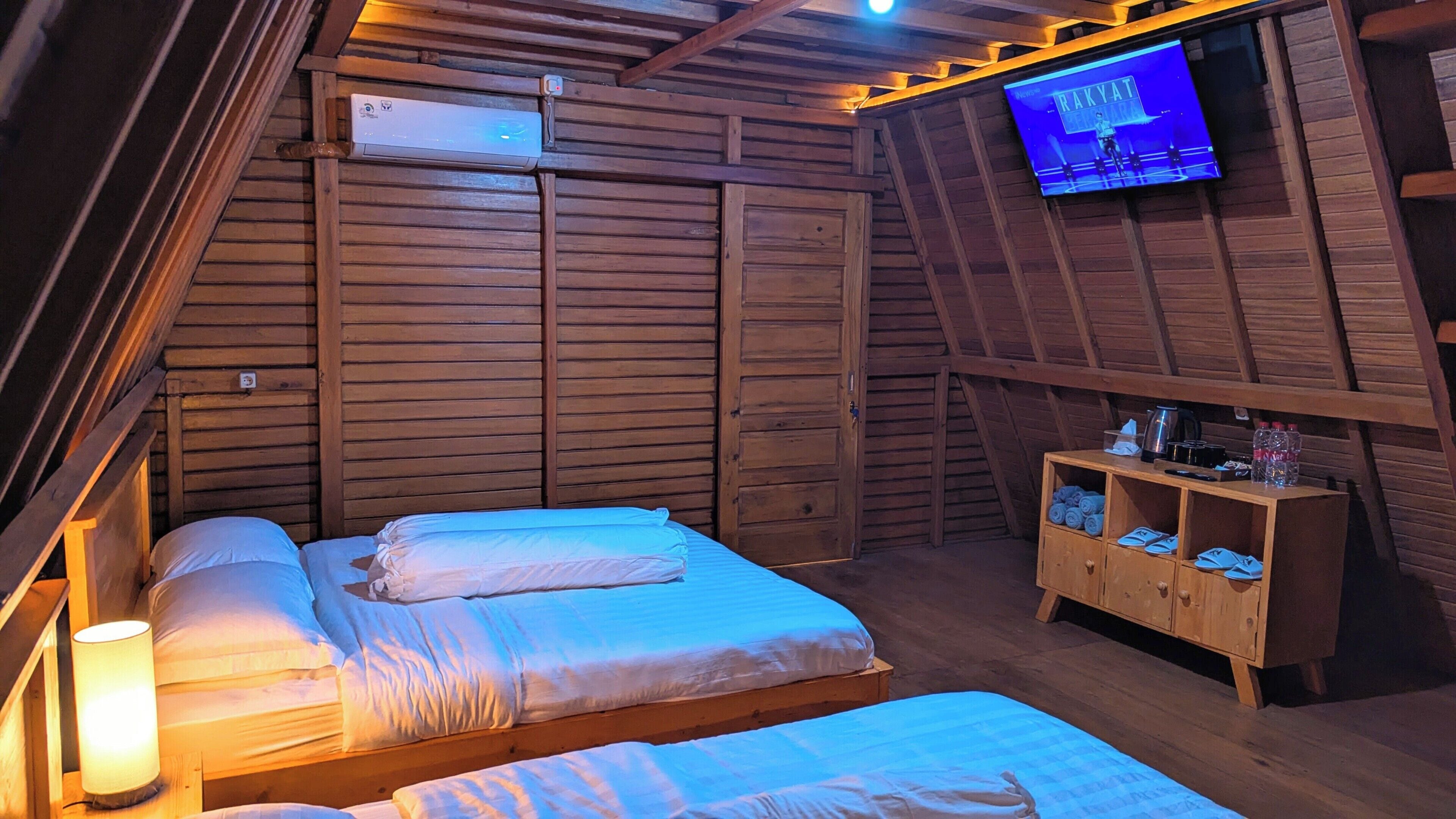 Quarto de sótão aconchegante com duas camas, uma televisão e um armário de madeira com artigos de higiene pessoal.