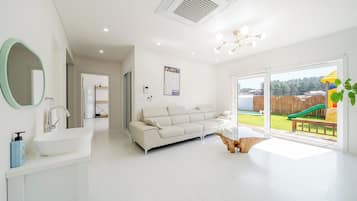 Uma sala de estar moderna com um sofá, uma mesa de centro de vidro e vista para um quintal com um escorrega.
