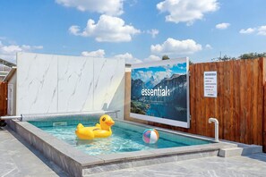 Piscina com cerca de madeira, uma tela grande exibindo uma paisagem e brinquedos infláveis.