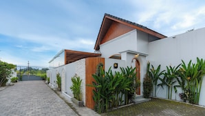Uma casa moderna com um caminho de acesso pavimentado, uma porta de madeira e uma parede exterior branca.