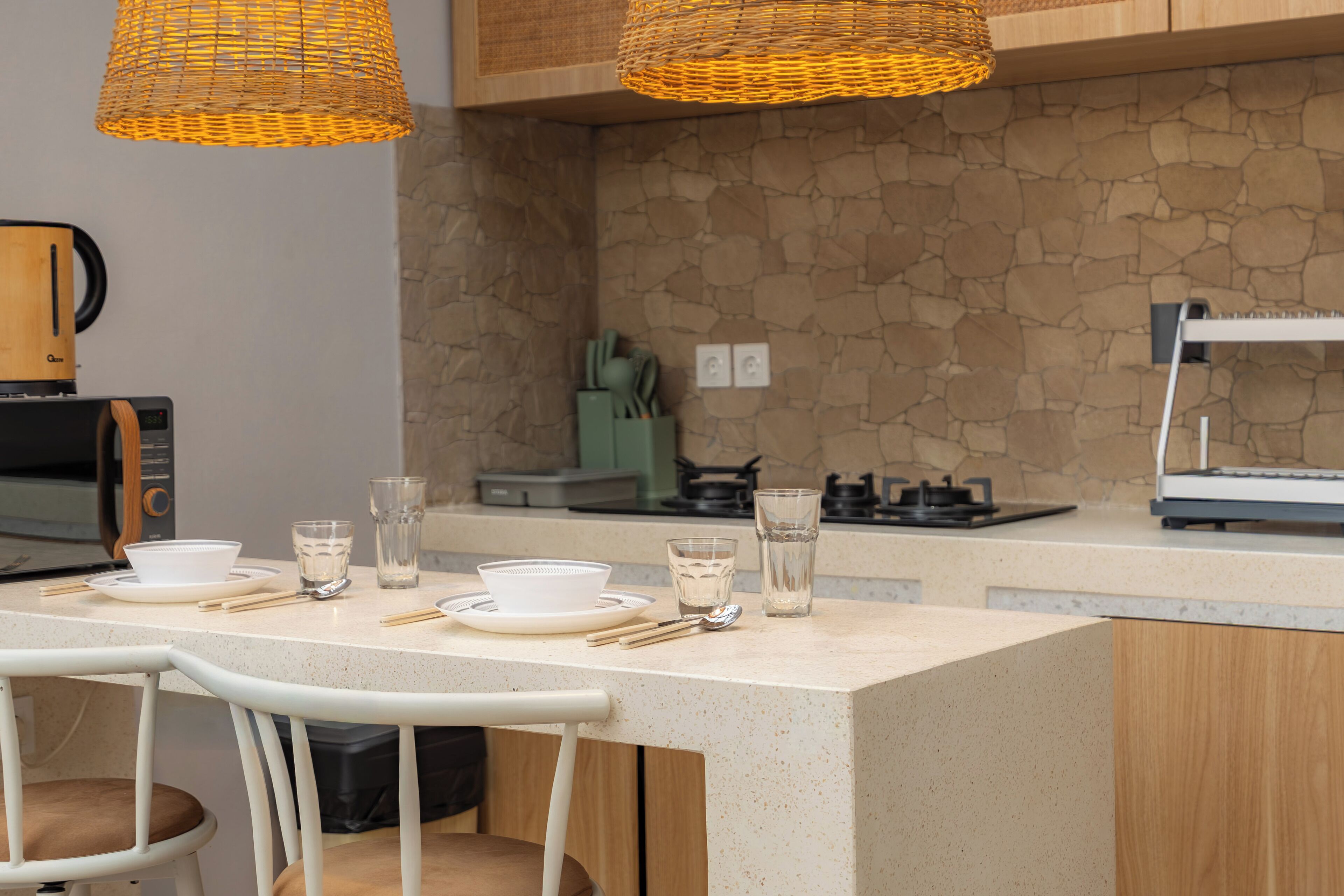 Uma cozinha com parede de pedra, bancada de madeira e luminária de vime suspensa.