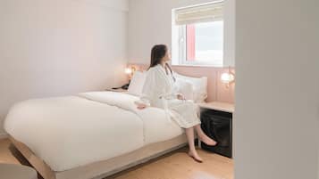 Uma cama de solteiro com estrutura de madeira, uma mesa de cabeceira com abajur e uma janela com persianas.