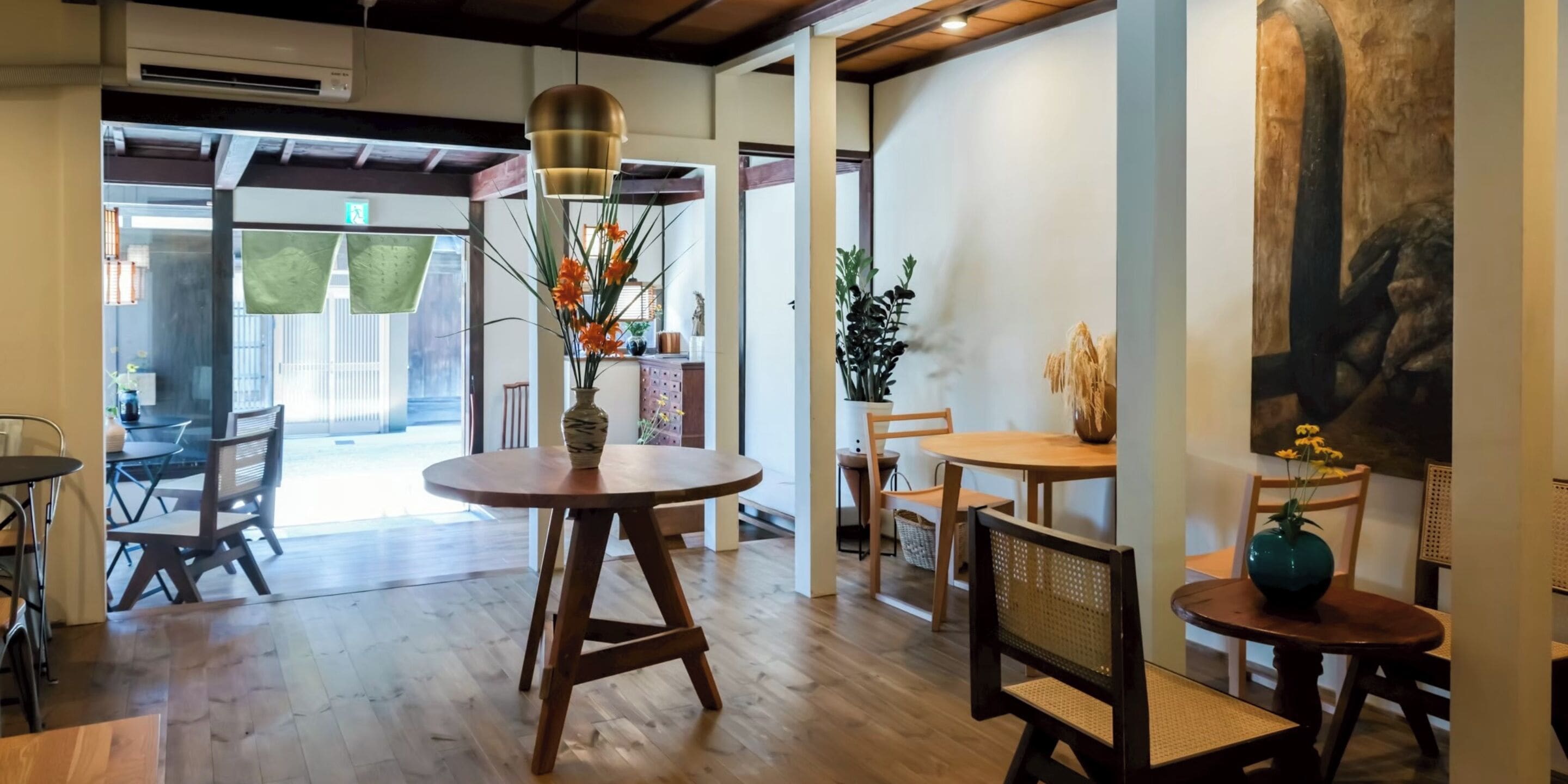 Um quarto espaçoso com piso de madeira, uma mesa redonda com cadeiras, uma luminária pendente e um quadro na parede.
