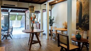 Um quarto espaçoso com piso de madeira, uma mesa redonda com cadeiras, uma luminária pendente e um quadro na parede.