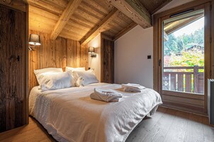 Quarto com painéis de madeira, uma cama, almofadas e uma janela com vista para o verde.