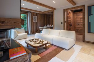 Uma sala de estar moderna com um sofá branco, uma mesa de centro e uma televisão. Teto de madeira e uma porta que dá para outro cômodo.