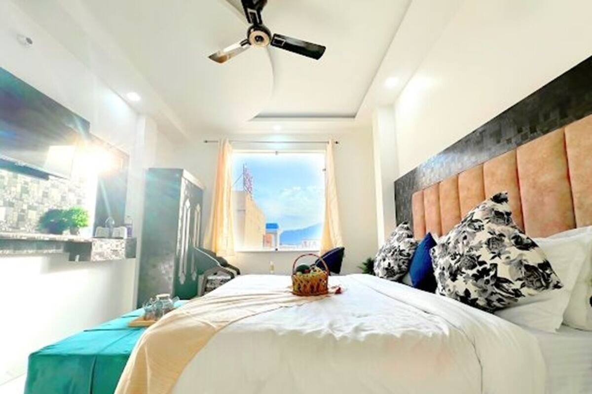 Quarto de hotel com cama, ventilador de teto, janela com vista e uma mesa cor de verde-água.