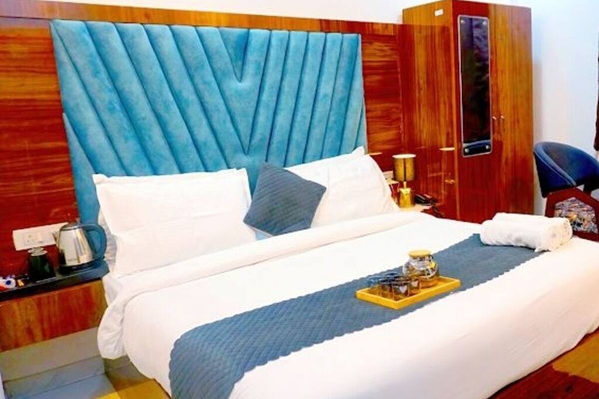 Quarto de hotel com uma cama grande, cabeceira de madeira, mesa de cabeceira com chaleira e guarda-roupa.