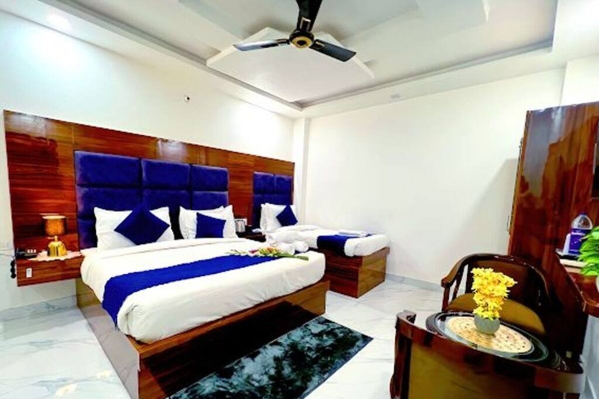 Quarto de hotel com cama, escrivaninha, cadeira, ventilador de teto e mesa de cabeceira.
