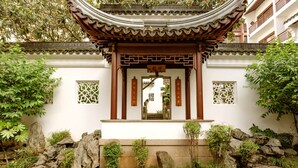Um portão chinês tradicional com desenhos elaborados, rodeado por um jardim com pedras e plantas.