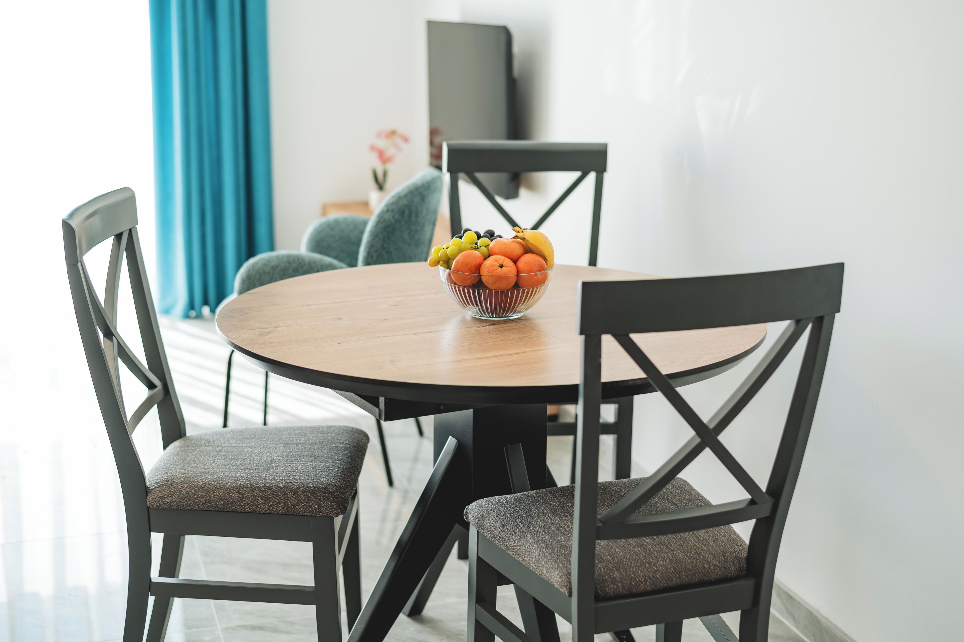 Uma mesa de jantar com uma fruteira, quatro cadeiras e uma televisão ao fundo.