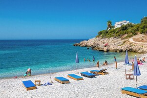 Uma praia com águas azul-claras, espreguiçadeiras e guarda-sóis.
