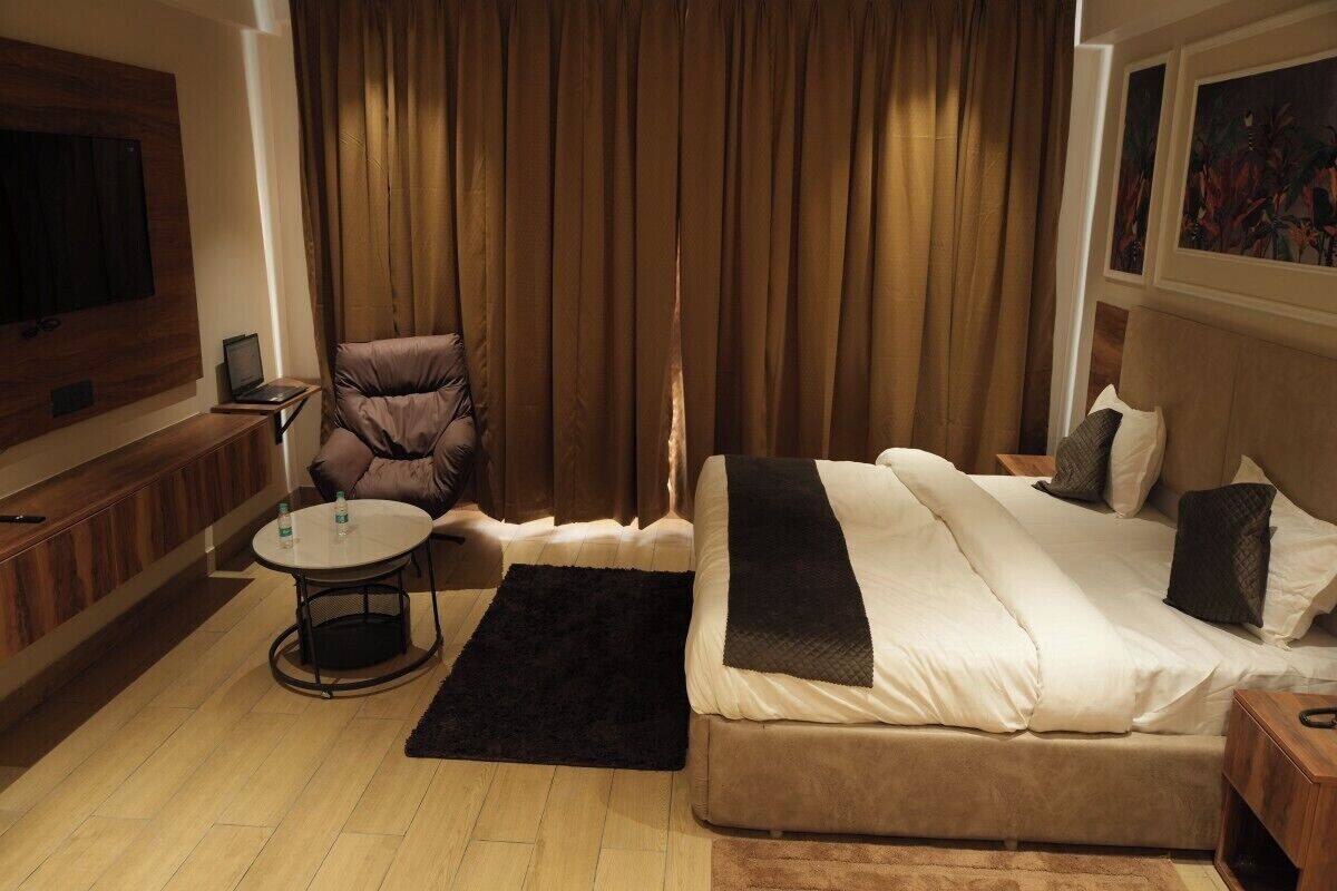 Quarto com cama, cadeira, mesa redonda pequena e televisão presa na parede.