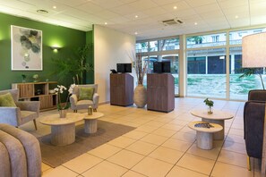 Um lobby moderno com sofás, uma mesa de centro, uma televisão e uma grande janela com vista para o exterior.