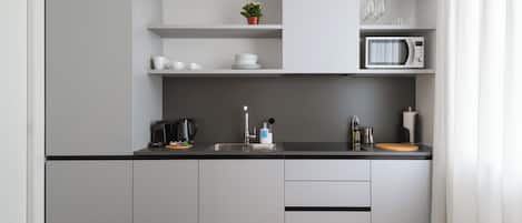 Uma cozinha moderna com armários cinza, bancada preta, micro-ondas e cafeteira.