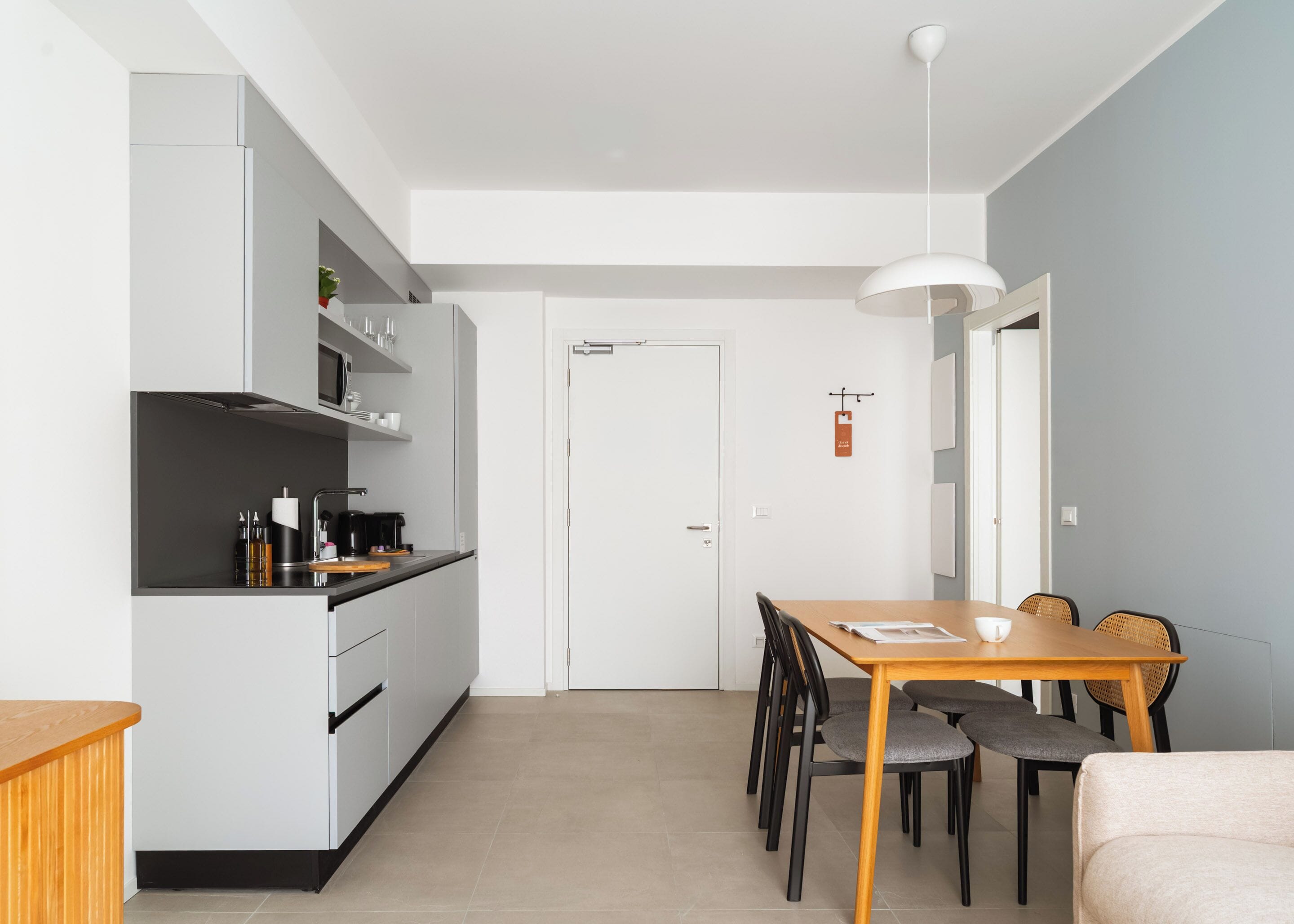 Uma cozinha moderna com armários brancos, bancada preta e uma mesa de jantar de madeira com cadeiras.