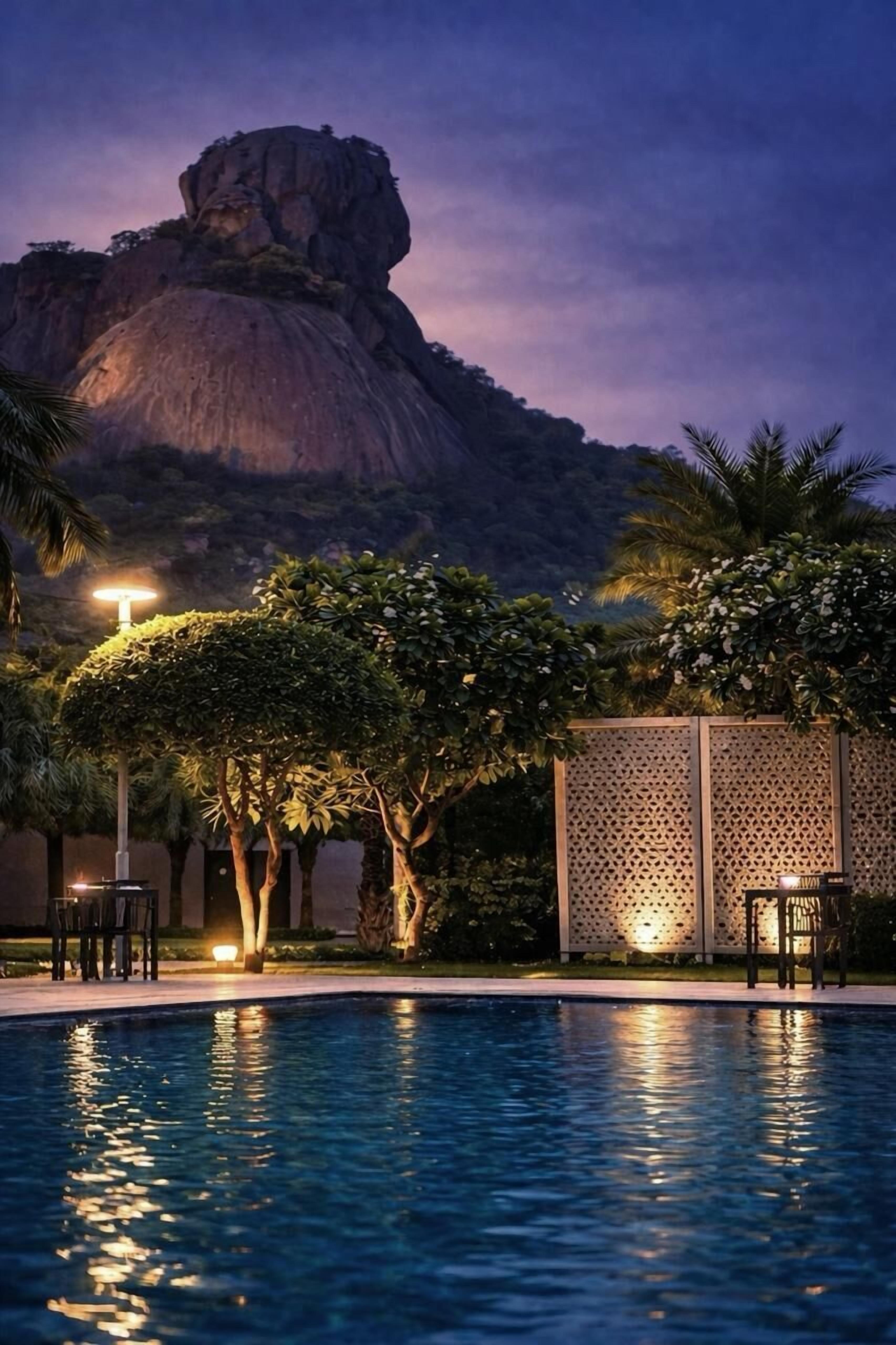 Piscina com vista para uma grande formação rochosa ao entardecer.