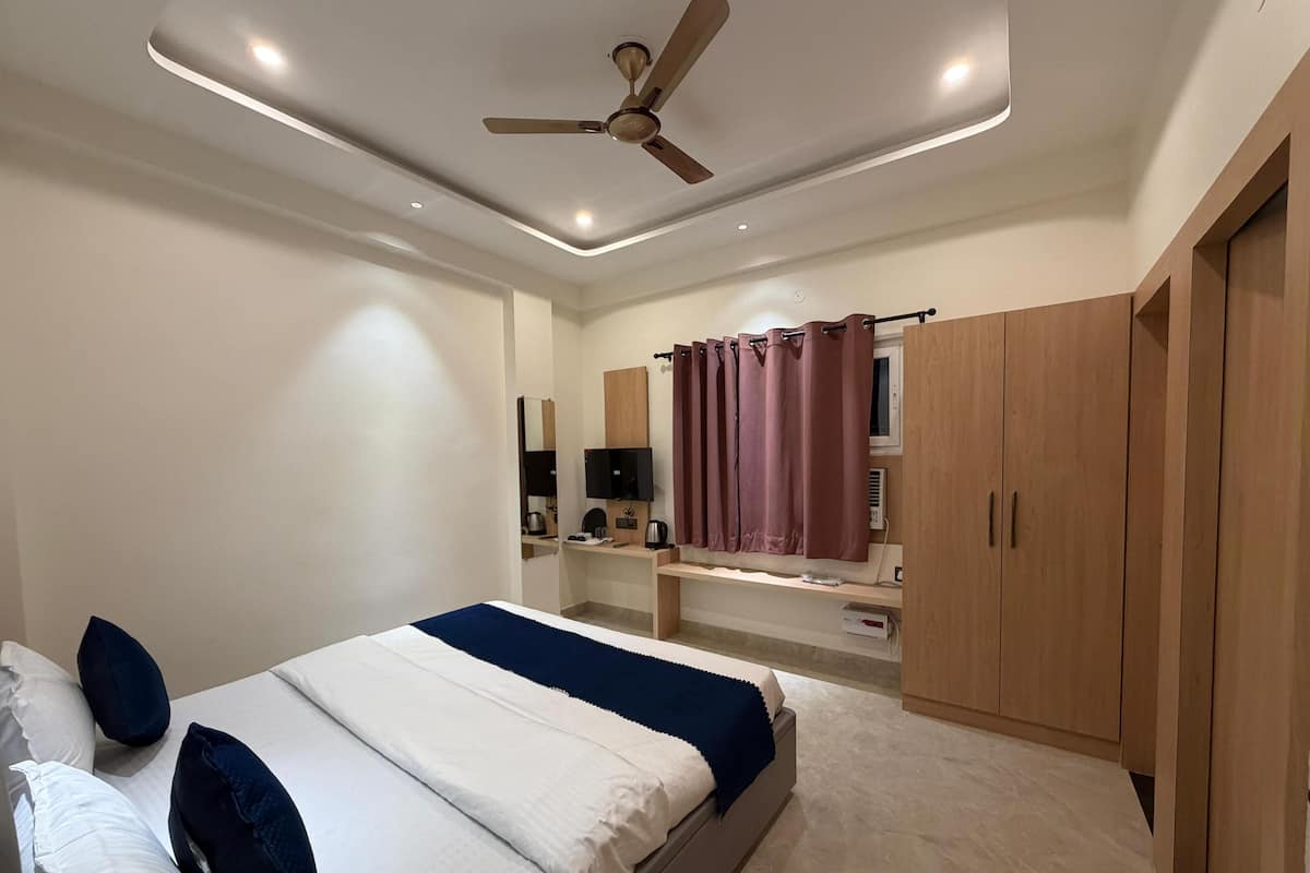 Um quarto com cama, ventoinha no teto, televisão, escrivaninha e guarda-roupa.