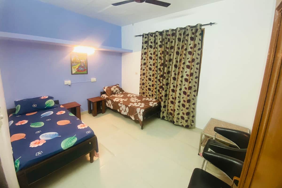 Quarto com duas camas, um ventilador de teto, uma mesinha e uma cadeira.