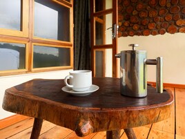 Uma mesa de madeira com uma chávena branca e uma cafeteira de metal.