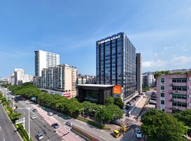 Um hotel moderno com uma placa grande, cercado por edifícios urbanos e uma rua movimentada.