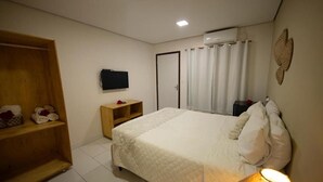 Quarto com cama, guarda-roupa de madeira, televisão e ar-condicionado fixado na parede.