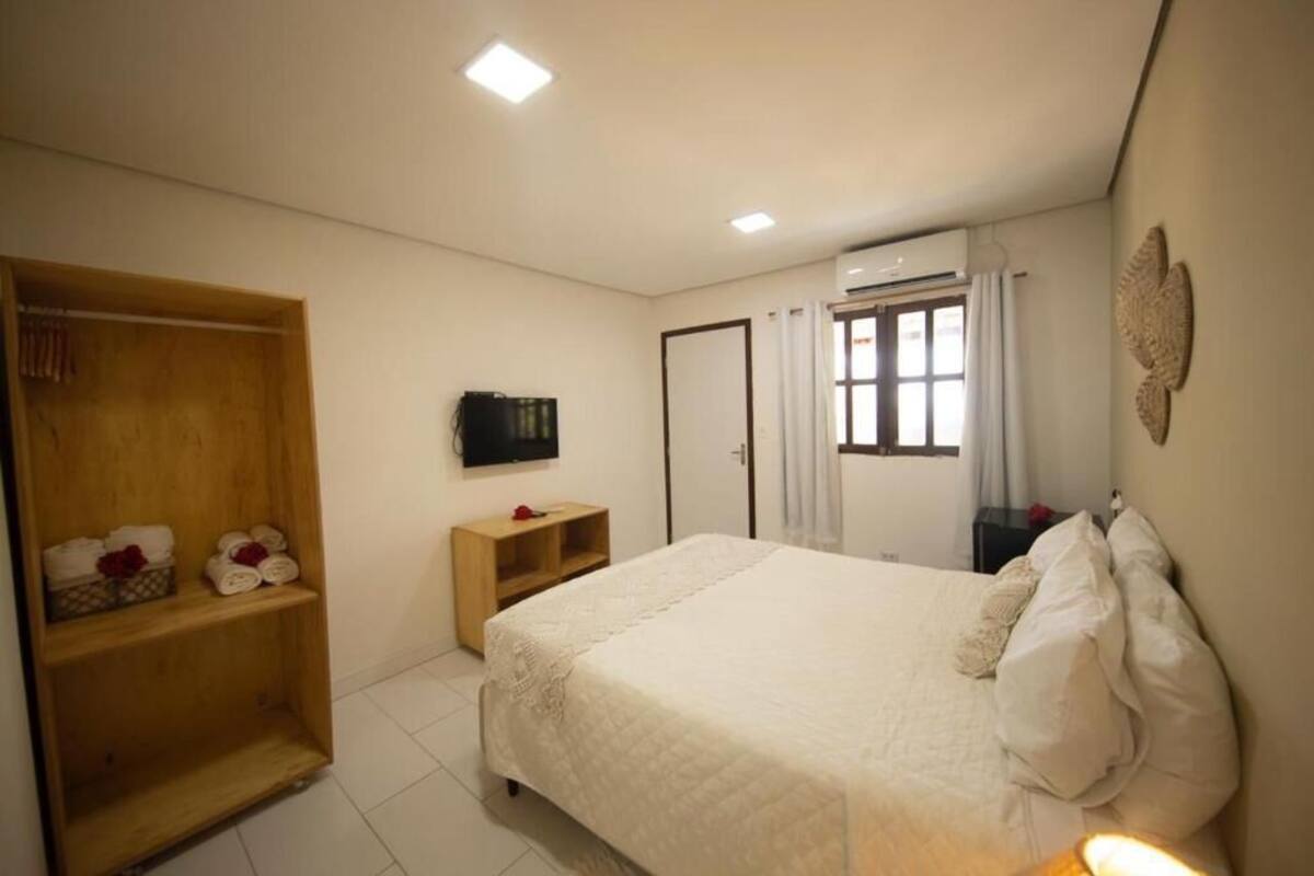 Um quarto com cama, guarda-roupa de madeira, televisão e janela com cortinas.