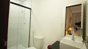 Uma casa de banho moderna com chuveiro, sanita, lavatório e espelho.