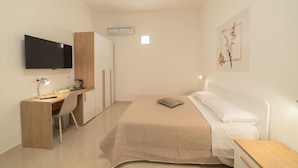 Quarto com cama, escrivaninha, cadeira, televisão e ar condicionado.