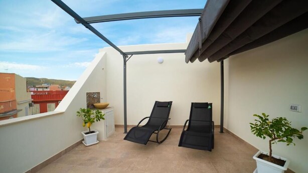 Terraço no telhado com duas cadeiras de descanso pretas, um vaso branco com planta e um armário branco.