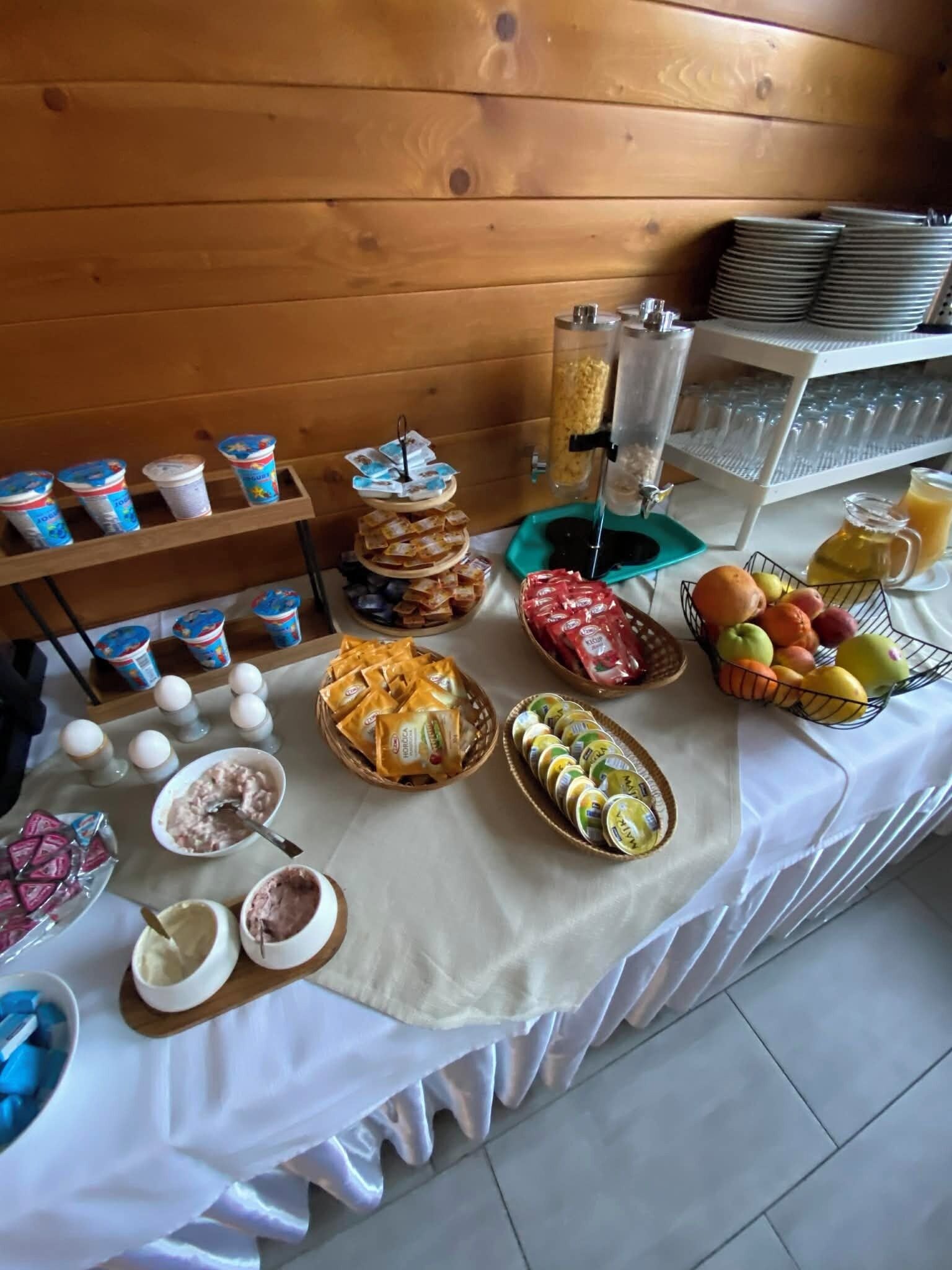 Uma mesa de buffet com diversos alimentos e bebidas, incluindo potes de iogurte, sanduíches e frutas.