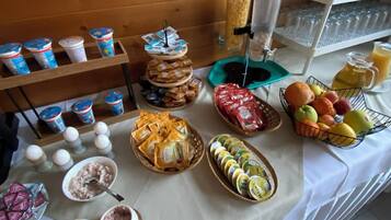 Uma mesa de buffet com diversos alimentos e bebidas, incluindo potes de iogurte, sanduíches e frutas.