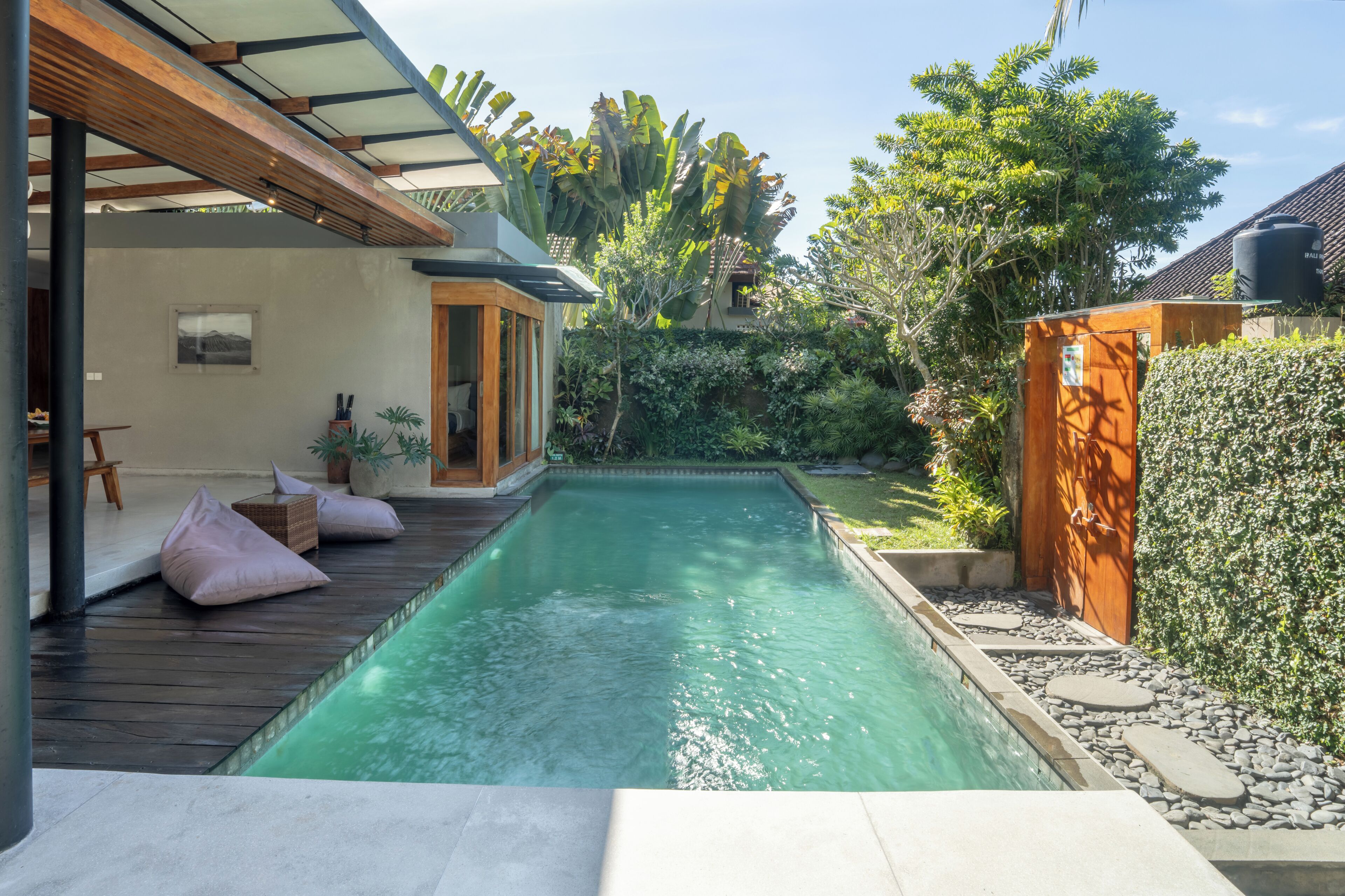 Piscina com deck de madeira, estrutura de madeira com portas de vidro e vegetação exuberante.