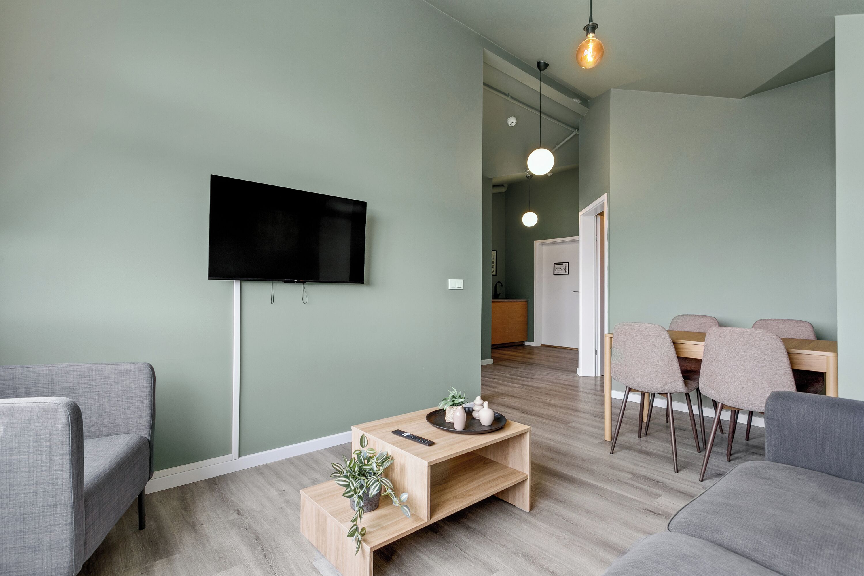 Uma sala de estar moderna com televisão de tela plana, uma mesa de centro com objetos decorativos, um sofá e uma área de jantar com cadeiras e mesa.