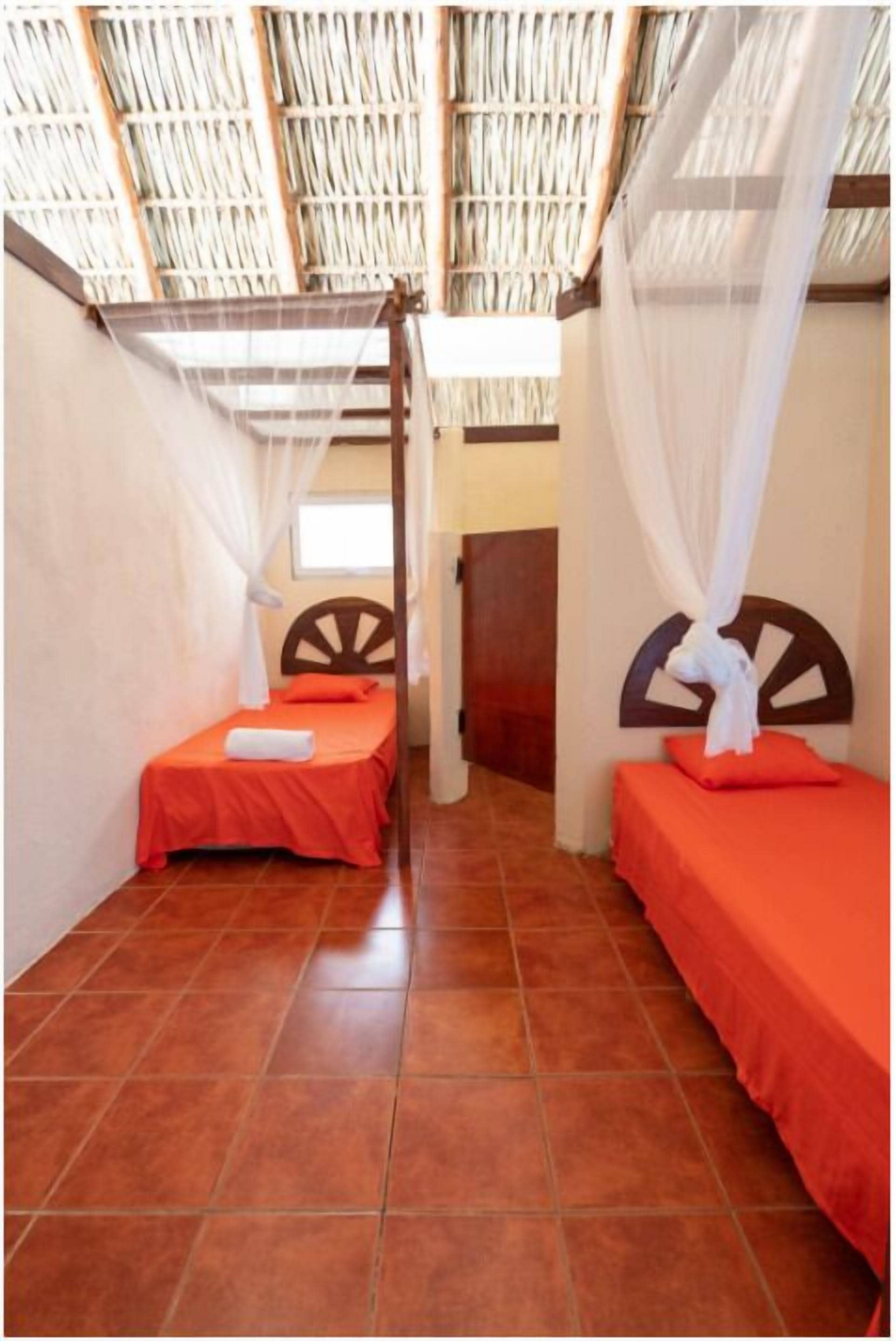 Quarto com duas camas, cabeceira de madeira, piso ladrilhado e teto com padrão trançado.