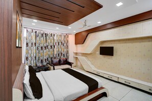 Quarto de hotel com cama, escrivaninha, cadeira, televisão e guarda-roupa.