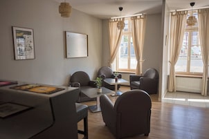Quarto moderno com mesa de jantar, cadeiras, uma pequena mesa com uma planta e grandes janelas com cortinas.