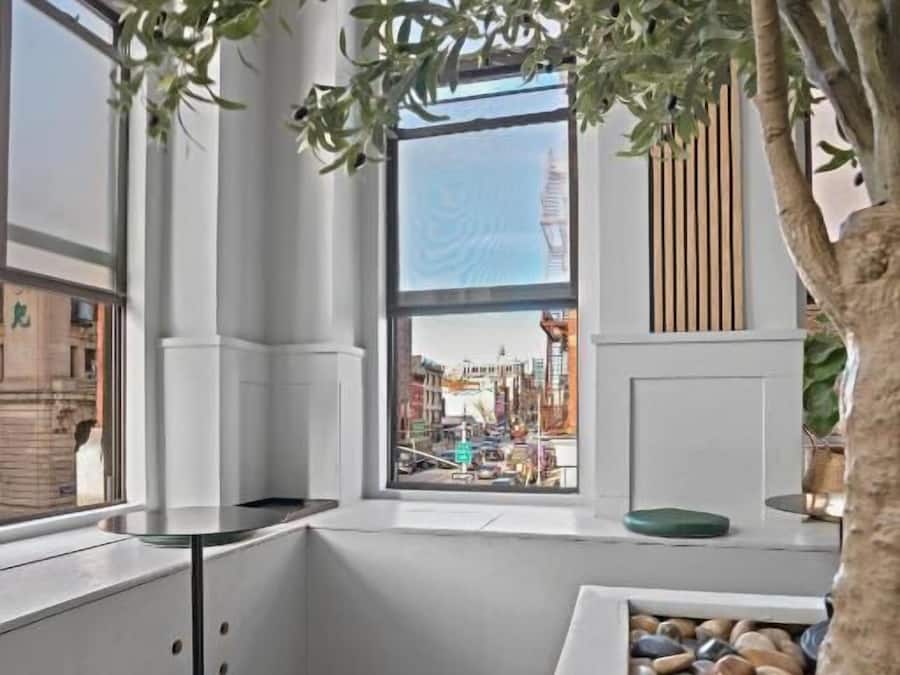 Um interior moderno com uma janela ampla, um vaso de plantas e vista para edifícios.