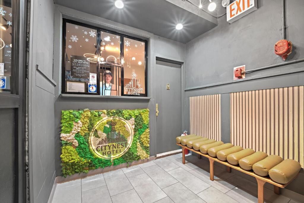Uma área de recepção com o letreiro Citynest Hotel, um banco e um sinal de saída.