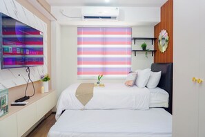 Quarto de hotel com cama, televisão fixada na parede, janela com persianas listradas e ar condicionado na parede.