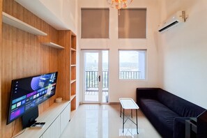 Uma sala de estar moderna com televisão de tela plana, um sofá escuro, uma mesa pequena e uma varanda com vista para a cidade.