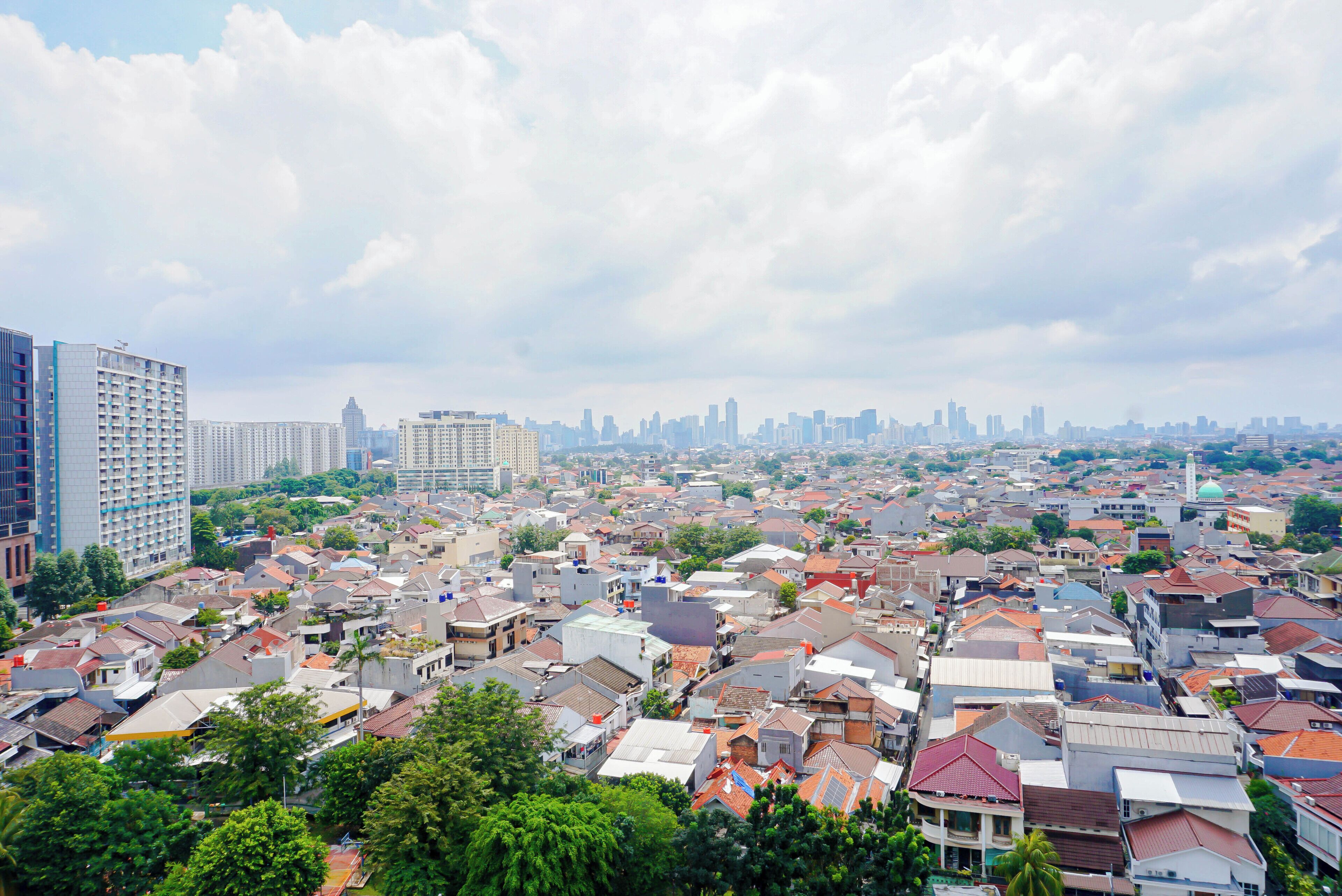 Paisagem urbana com mistura de edifícios residenciais e comerciais, incluindo apartamentos altos e casas menores, sob um céu parcialmente nublado.