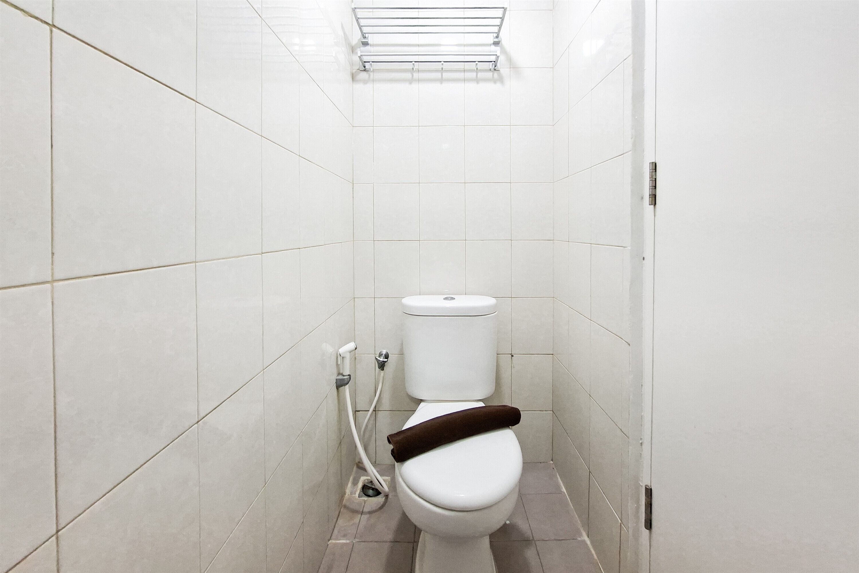 Uma casa de banho pequena, com azulejos brancos, um autoclismo, um suporte para toalhas e um rolo de papel higiénico.