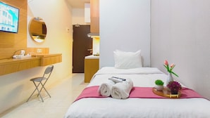 Quarto de hotel com uma cama, escrivaninha com cadeira, televisão, espelho e porta para o banheiro.
