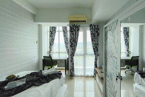 Quarto de hotel com uma cama, uma escrivaninha, uma cadeira e um espelho grande.